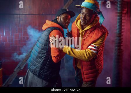 Two stylish rappers with gold jewelry in cool studio, yellow background ...