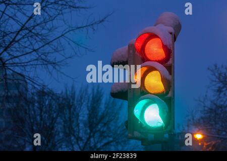 Snow-covered traffic lights switched to red, pedestrian lights at dusk ...