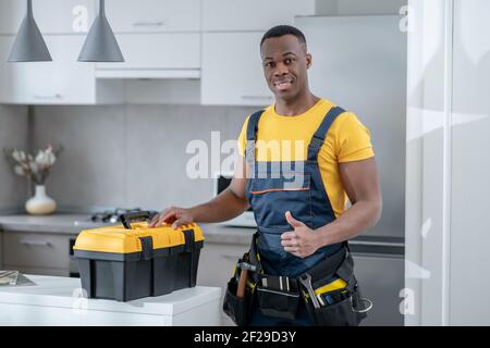 Dark-skinned service man standing in the kitchen and holding a box with ...