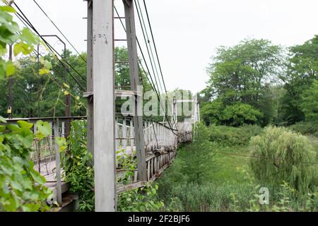 Old iron non-functioning suspension bridge over a dried river side view ...