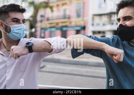Handsome Spanish men wearing masks and greeting each other with elbows ...
