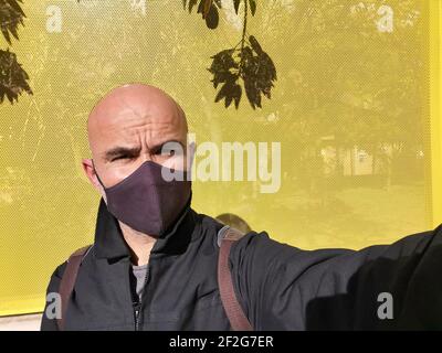 A bald handsome Spanish man with a mask in the street on a yellow ...