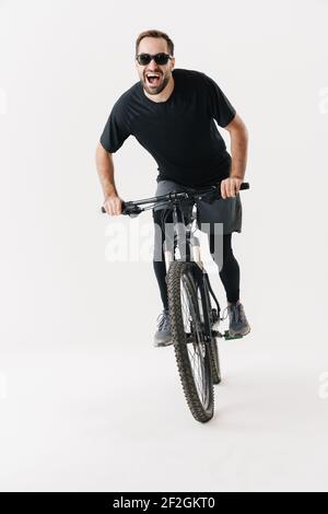 Excited young sportsman in sunglasses riding his bicycle isolated over ...