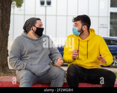 A closeup of two Spanish Caucasian men, sitting outdoors and talking ...