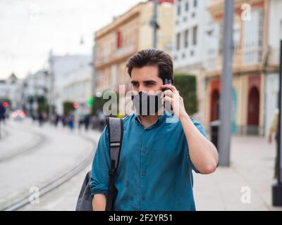 A Spanish male with face mask talking on the phone outdoors - concept ...