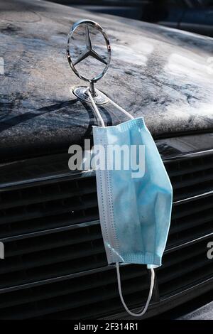 A face mask hangs from the star of a mercedes car Stock Photo - Alamy