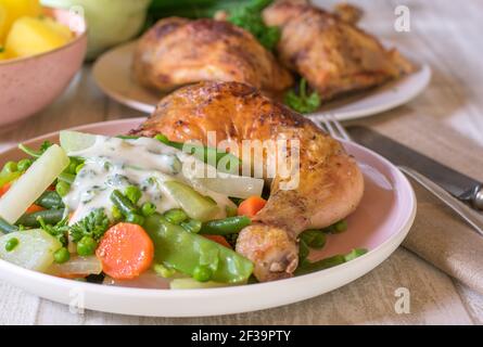Golden roasted chicken leg on white plate surrounded by green onions ...