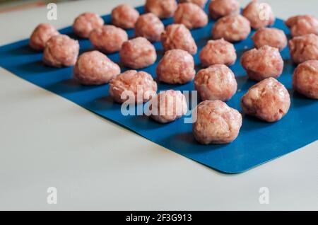 Raw shaped meatballs on blue. Rows of meatballs with pepper, salt and ...