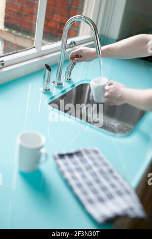 Washing glass cup under tap with flowing water in a light-filled ...