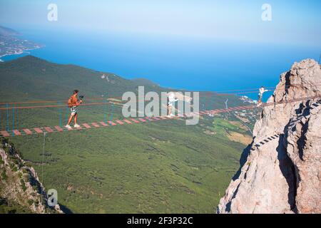 Family crossing the chasm on the rope bridge. Black sea background ...