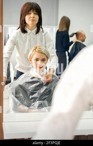The female hairdresser puts on a transparent cellophane cape to the ...