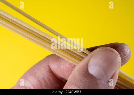 some uncooked spaghetti between the fingers of the hand Stock Photo - Alamy