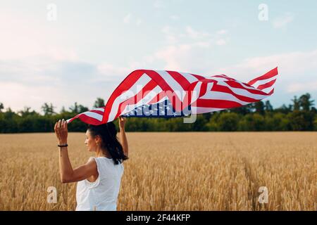 Woman with American flag in wheat field at sunset. 4th of July ...