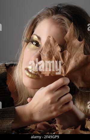 An Argentinian Blonde woman with bright gold makeup and dried leaves in ...