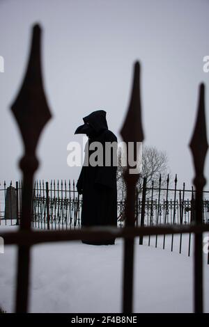 Medieval plague doctor stands on winter field with scythe in pandemic ...