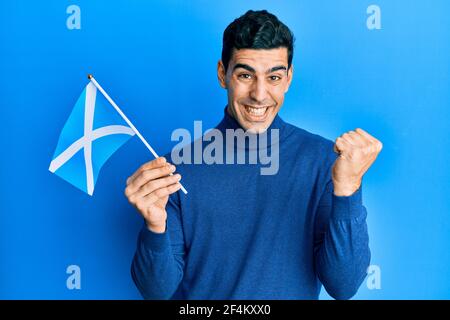 Handsome hispanic man holding scotland flag smiling happy pointing with ...