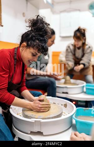 Concentrated female artisan in apron measuring wooden plank with measuring roulette while ...