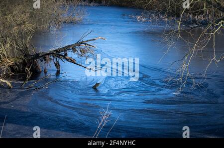 A beautiful picture of a small pond covered with ice. Blue icy water ...