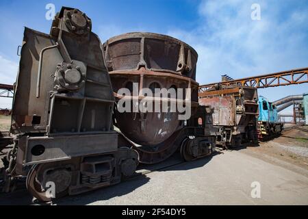 Metal alloys plant. Blue locomotive and rusted slag car wagons ...