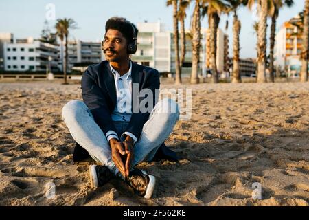 Thoughtful man listening music while sitting on floor in living room ...