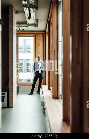 Businessman standing against office window reading documents Stock ...