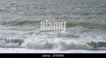 Waves of a choppy sea seen braking on the shoreline of an English beach ...