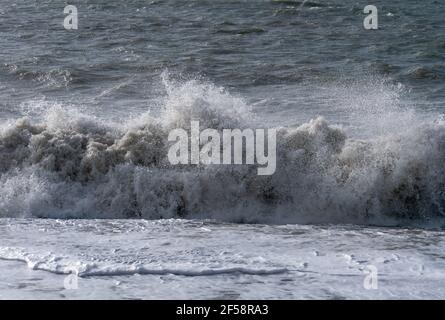 Waves of a choppy sea seen braking on the shoreline of an English beach ...