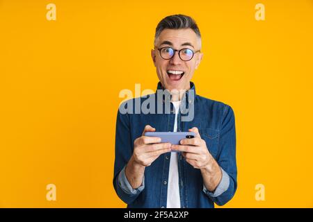 Delighted handsome man playing online game on mobile phone isolated ...
