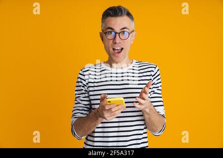 Excited handsome man exclaiming while using cellphone isolated over ...