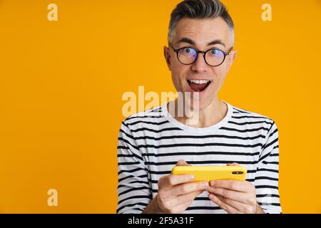 Delighted handsome man playing online game on mobile phone isolated ...
