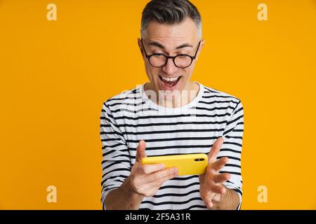 Delighted handsome man playing online game on mobile phone isolated ...