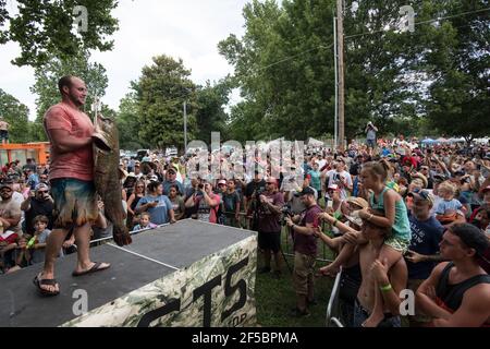 A triumphant noodler proudly displays his catfish to a cheering crowd ...