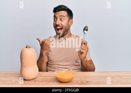 Handsome hispanic man eating pumpkin soup with spoon smiling happy ...