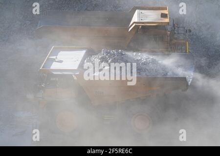 Dusty conditions as digger loads dump truck with ore at gold mine in ...