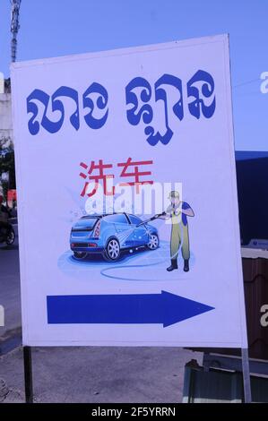 sign written in Khmer script in front of tropical vegetation. Nonmony ...