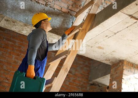 Builder man climbing up ladder on scaffold tower around dormer rooms ...