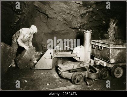 Miners load a boulder on a compressed air -powered loading machine ...