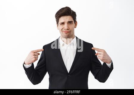 Doubtful businessman smiling skeptical, pointing and looking aside at ...