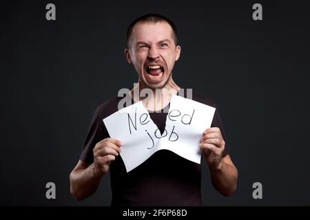 Sheet of paper with inscription I need a job in male hand on dark ...