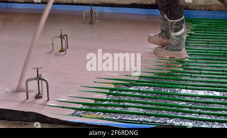 Workman pouring pumped anhydrite self levelling screed over underfloor ...