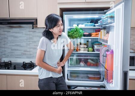 starving young asian woman hold her belly while open the fridge door ...