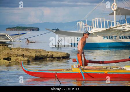 Filipino fisherman smiling as he prepares to take his outrigger canoe ...