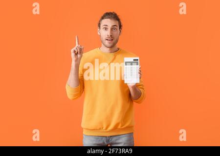 Young man with calculator and raised index finger on color background ...