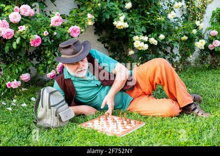 Old man in spring rosesgarden with chess. Hobby concept. Happy old age ...