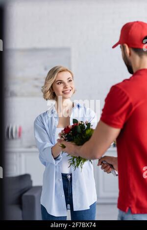 Young delivery woman giving bouquet of beautiful roses on yellow ...