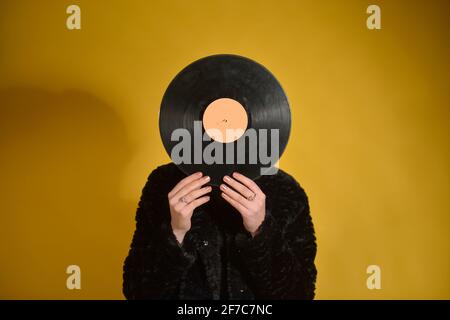 unrecognizable girl face covered with vynil record on yellow background ...