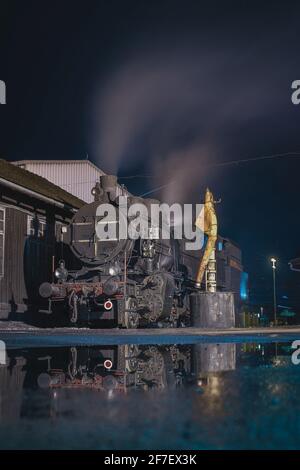 Old steam locomotive being fired up in front of a shed during the night ...