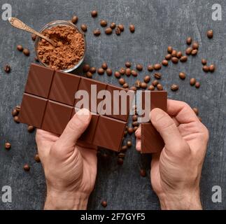 closeup man hands breaking dark chocolate block with knife on wood ...