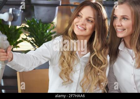 Smiling young girlfriends doing make-up at table in home interior Stock ...