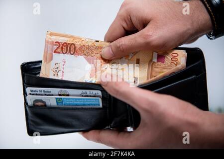 Men's hands holding wallet with Qatari notes. 200 Rial new notes ...